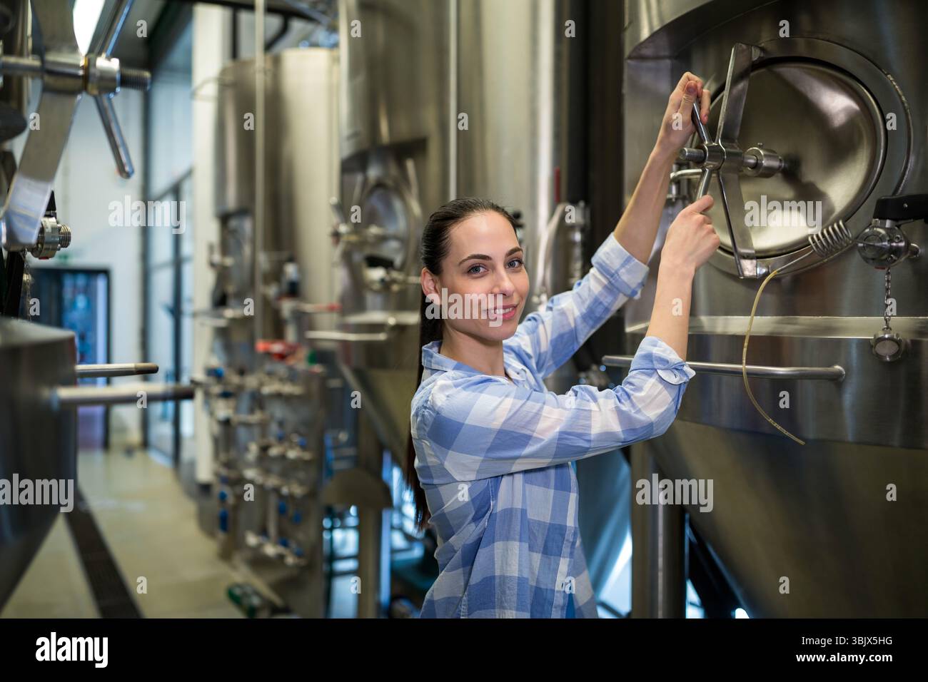 Female brewer adjusting latch on stainless steel fermentation tank amid ...