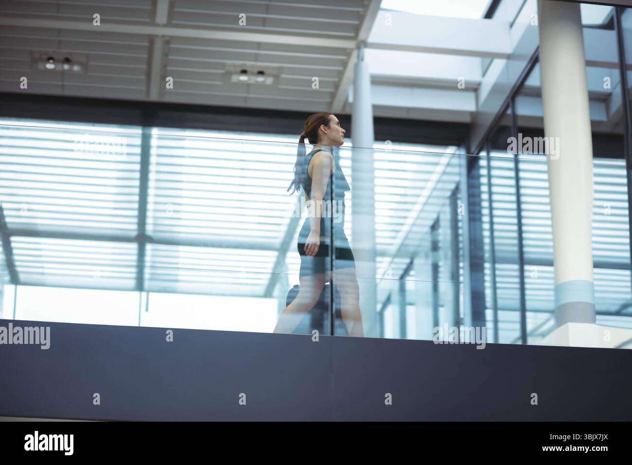 Woman walking in athletic attire on glass walkway inside terminal with ...