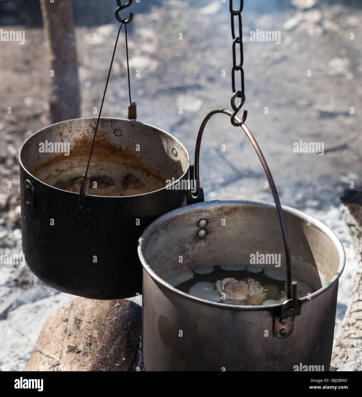 Cooking in two sooty old cauldrons on campfire Stock Photo - Alamy