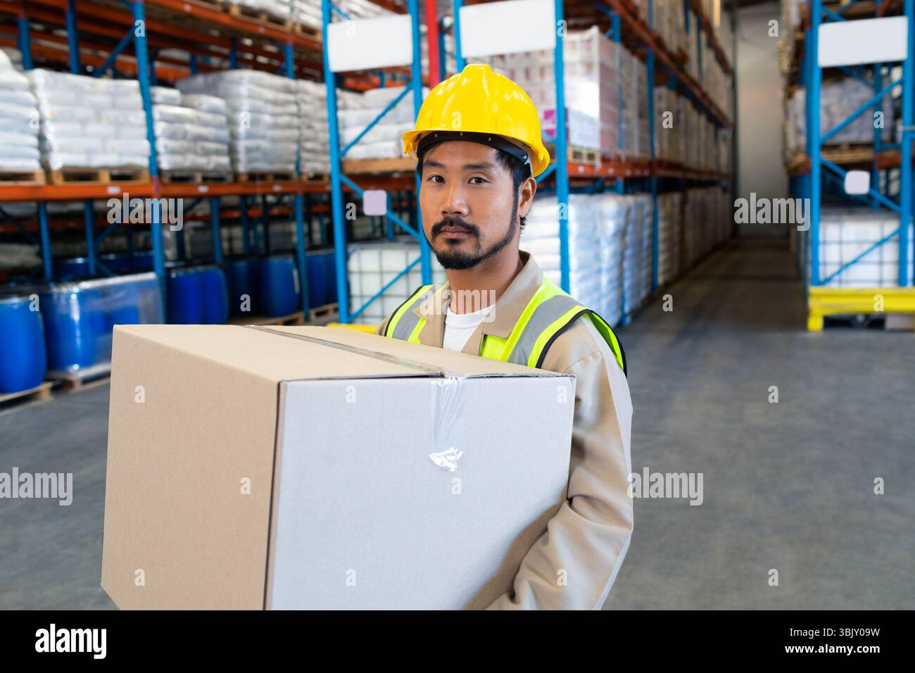 Asian male warehouse worker wearing safety vest holding cardboard box ...