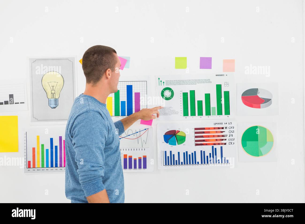 Single man pointing at green bar graph on white office wall with charts ...