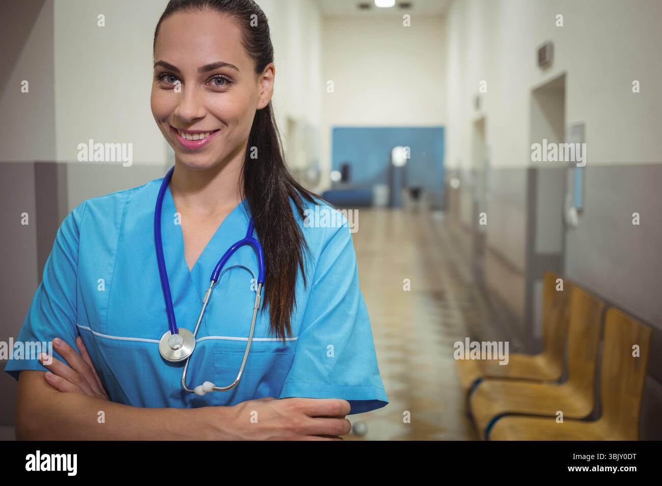 Female nurse standing with arms crossed smiling in hospital corridor ...