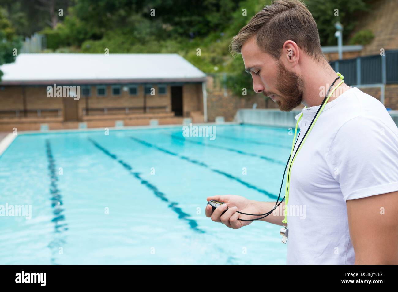 Male coach holding stopwatch and checking display standing poolside ...