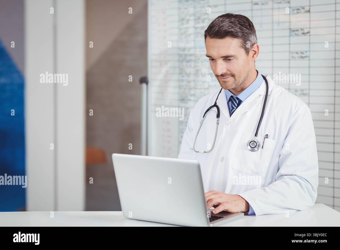 Doctor typing on silver laptop at desk with stethoscope and schedule ...