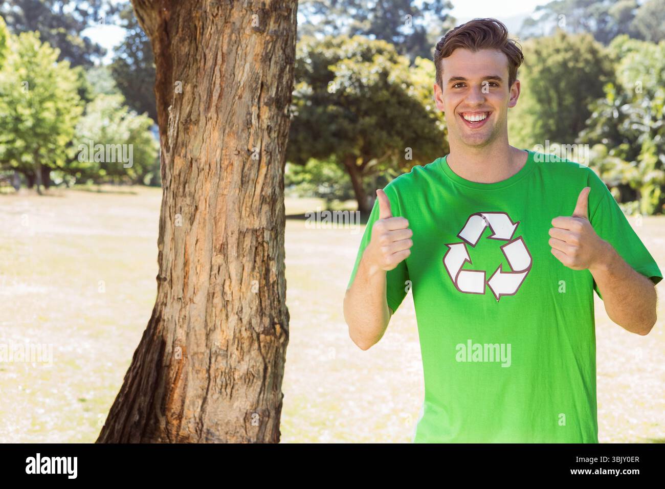 Man standing beside tree trunk in park wearing green recycling T-shirt ...