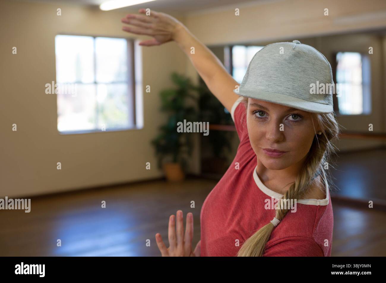 Female dancer wearing gray cap practicing pose by ballet barre before ...