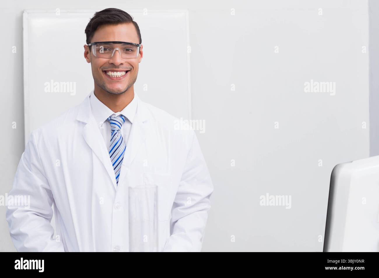 Male scientist wearing lab coat and safety glasses in lab, holding ...