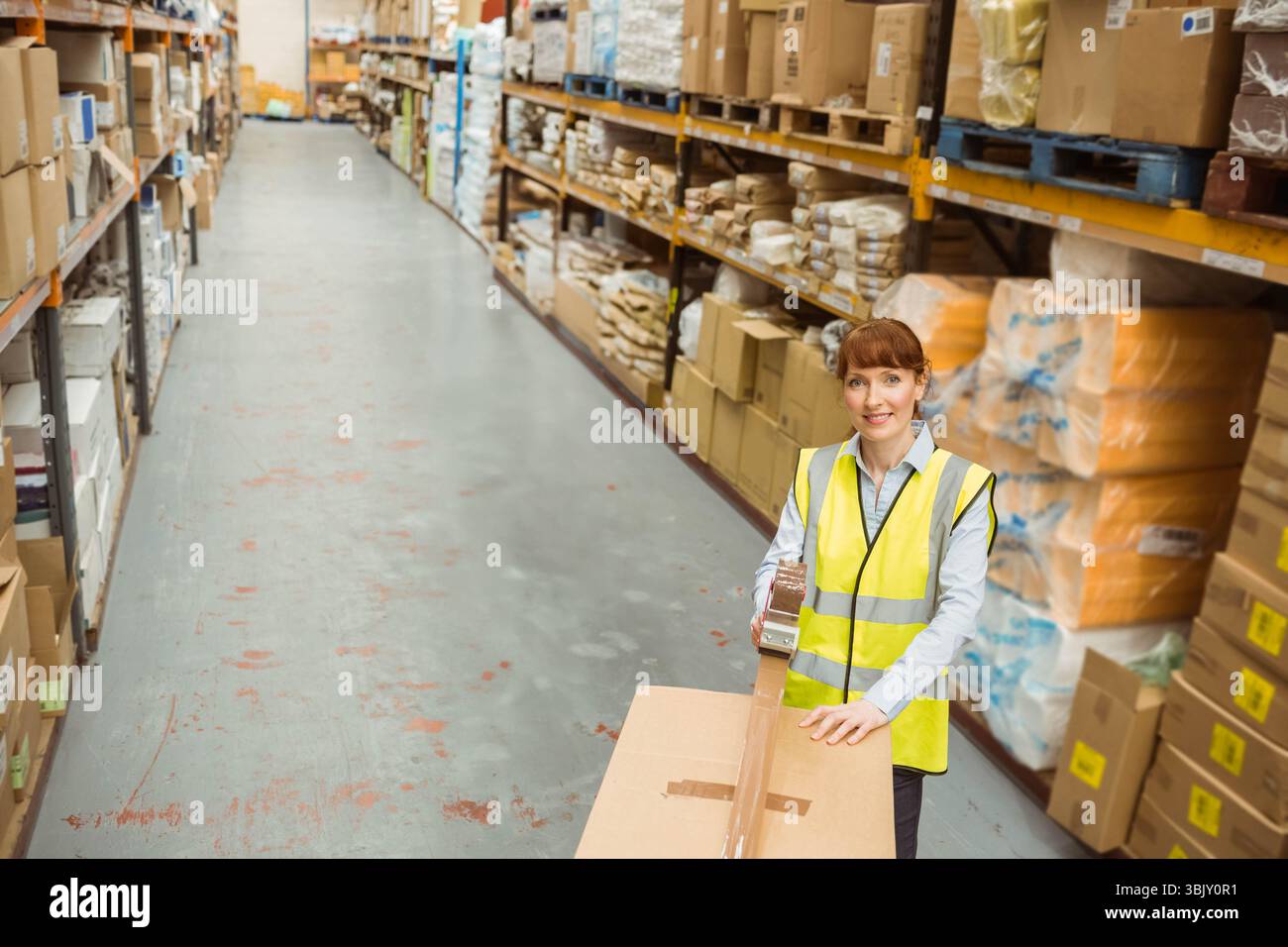 Female warehouse worker applying packing tape onto box in warehouse ...