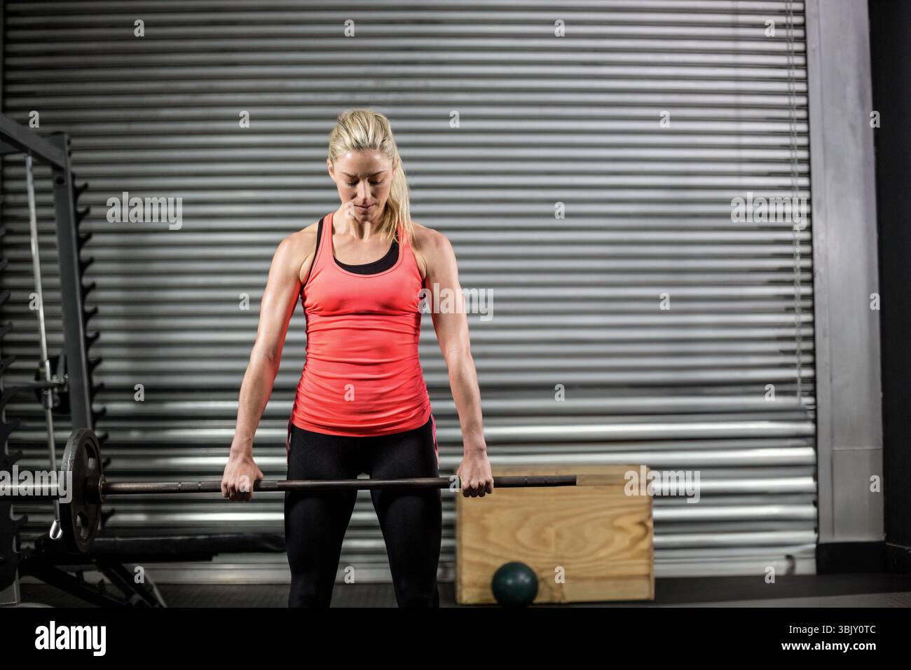 Mid-adult woman in sportswear holding loaded barbell at thigh level in ...