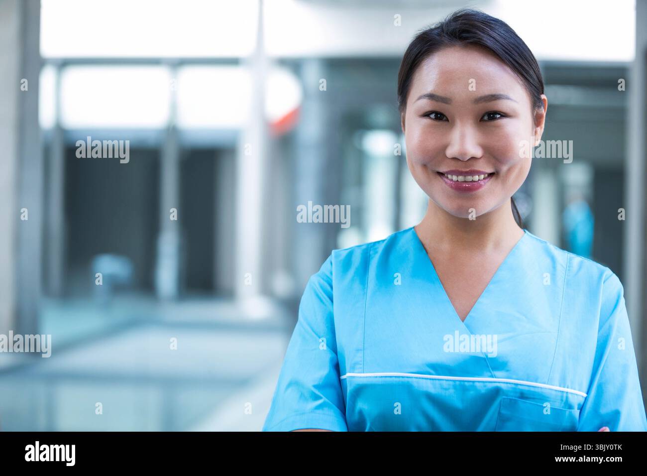 Asian woman nurse standing in modern hospital corridor wearing teal ...
