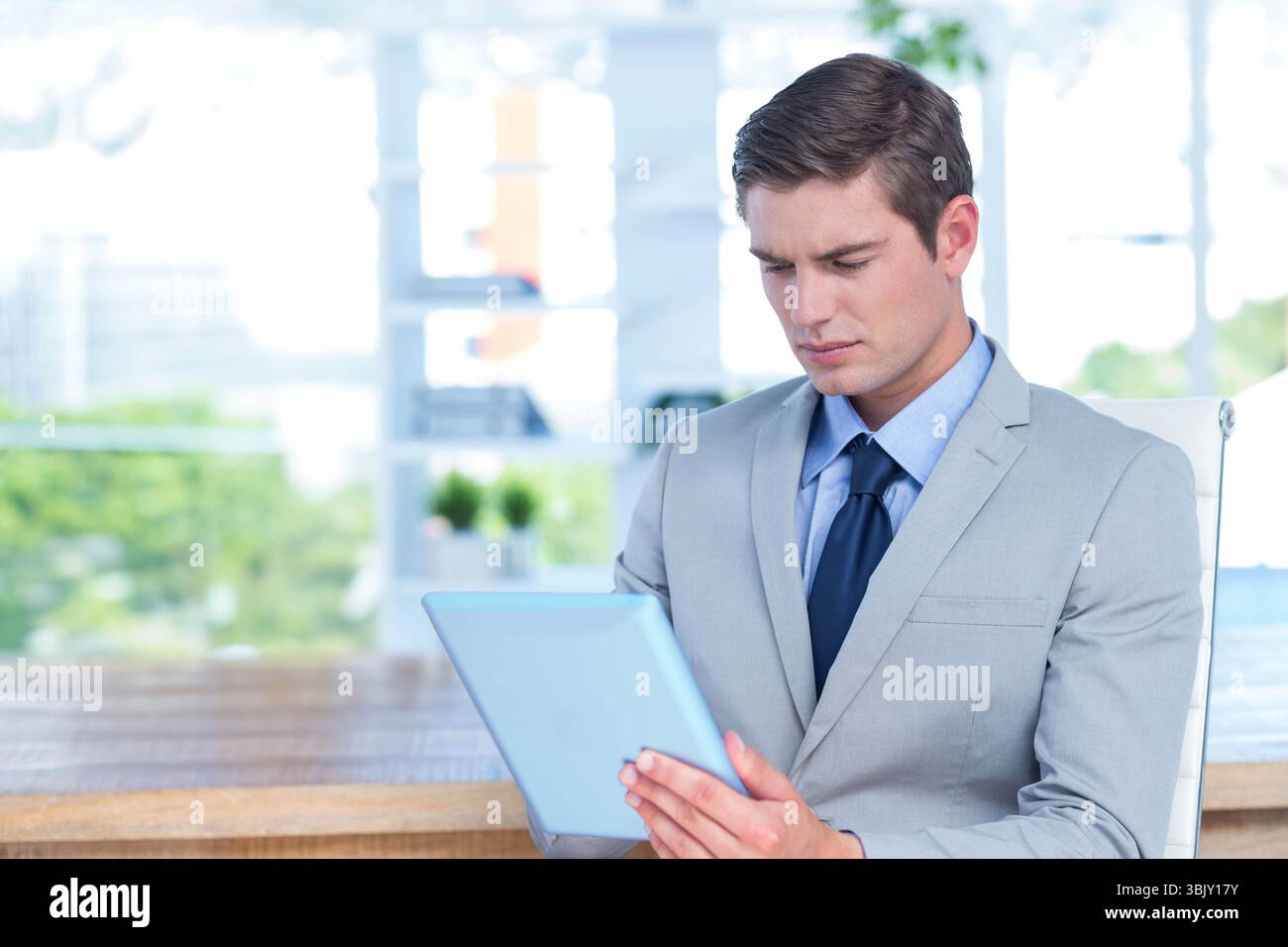 Business professional holding tablet and gazing at screen at desk in ...