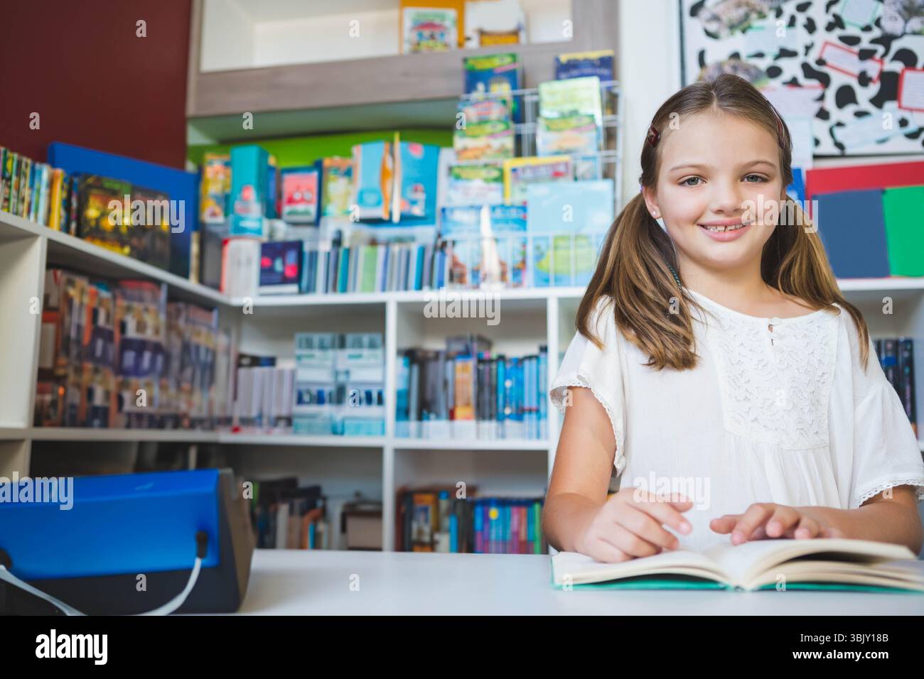 Female child sitting at library desk reading open book with white ...