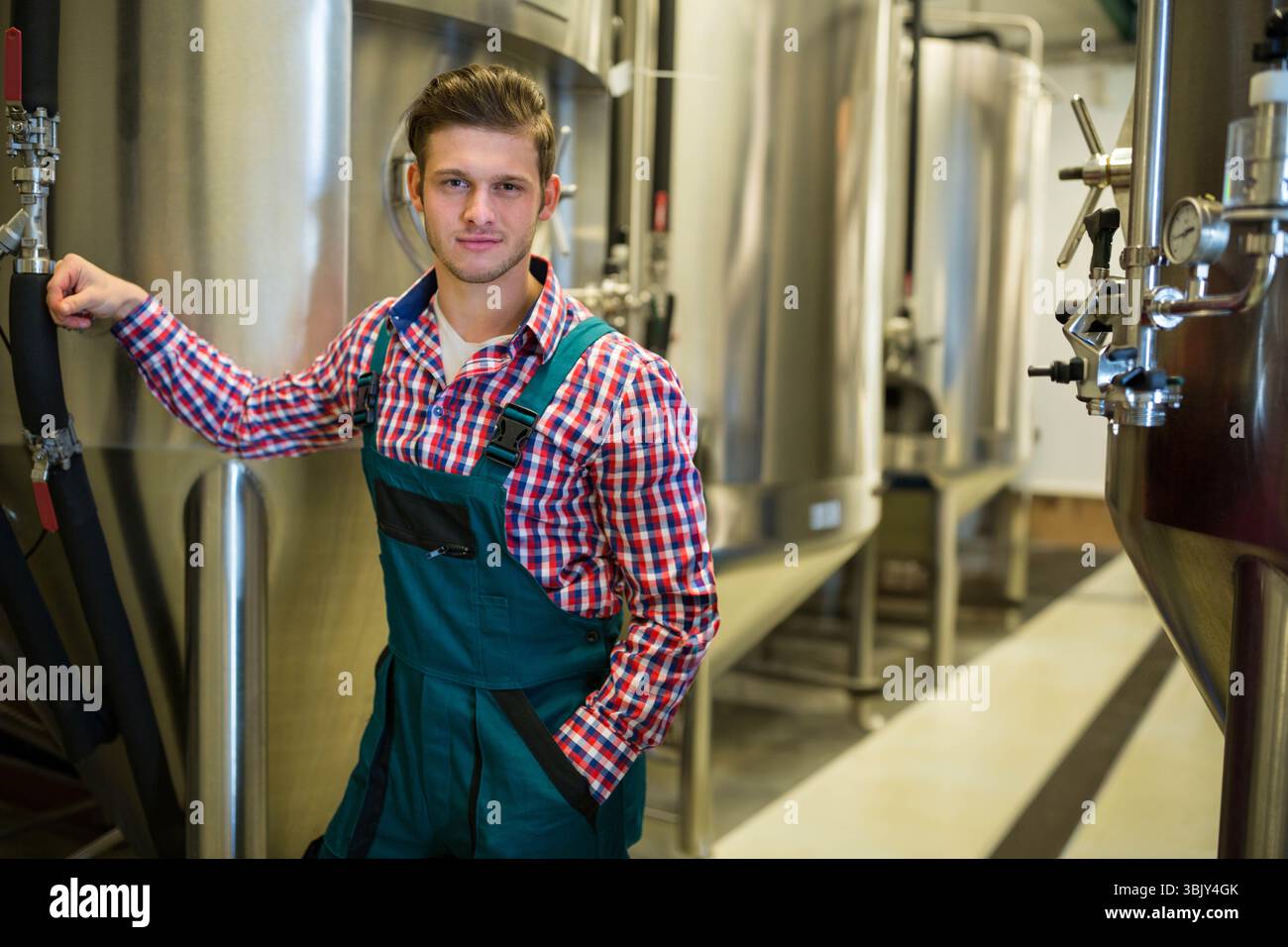 Male brewery worker in overalls standing near fermentation tanks at ...