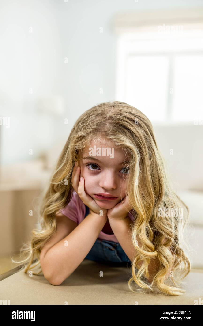 Child leaning on table resting chin and gazing at camera beside white ...