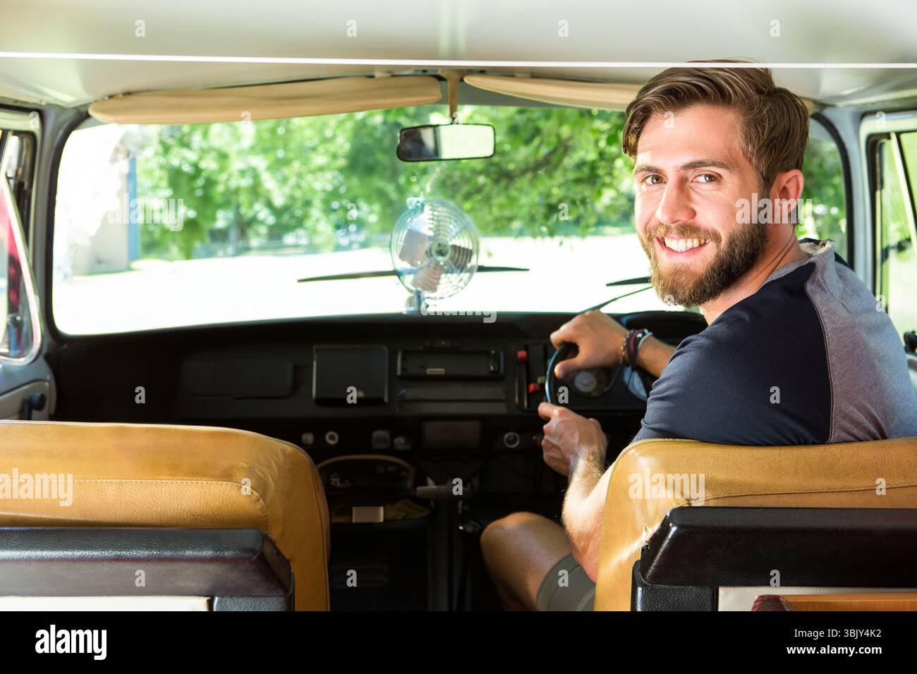 Man sitting in vintage camper van driver seat adjusting clip-on fan ...