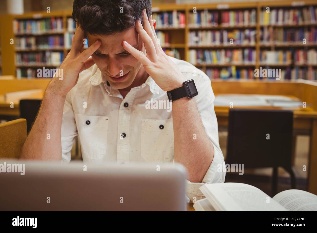 Student pressing temples at study table with open books, laptop and ...