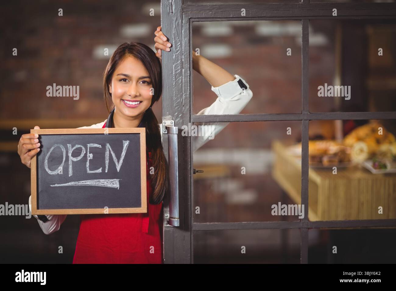 Shop assistant wearing red apron opening glass door at bakery entrance ...
