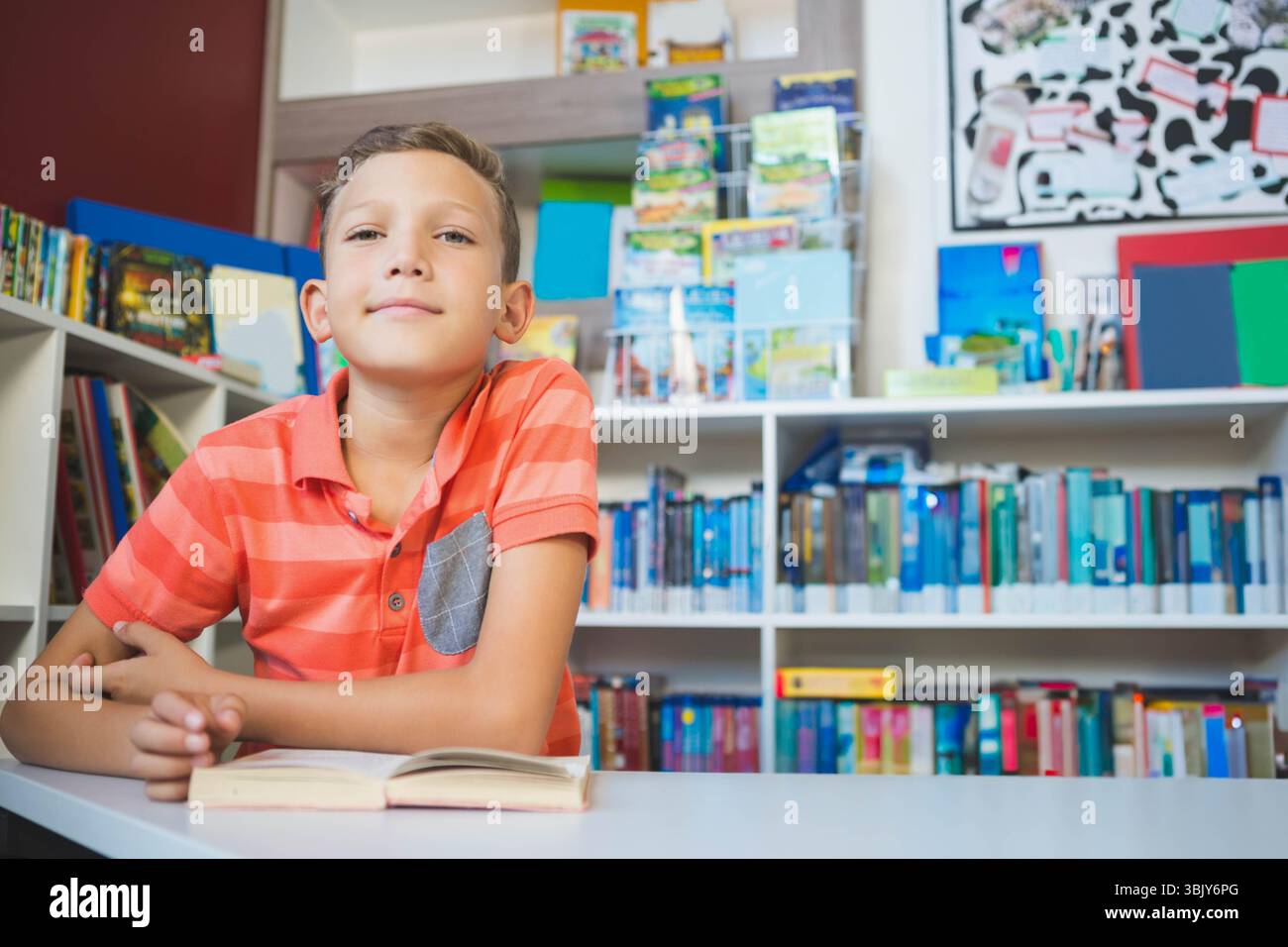 Boy reading open book at white table in school library reading corner ...