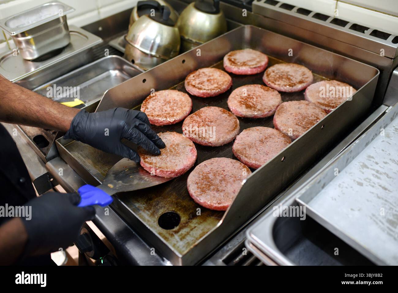 Chef cooking hamburgers on a hot professional griddle in a fast food ...