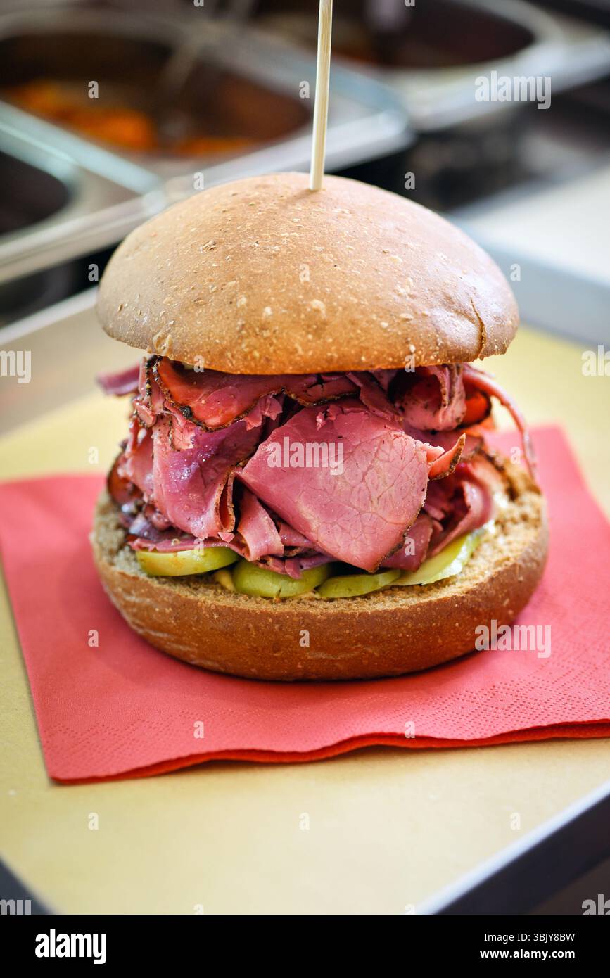 Whole wheat pastrami sandwich with pickles and meat slices held ...