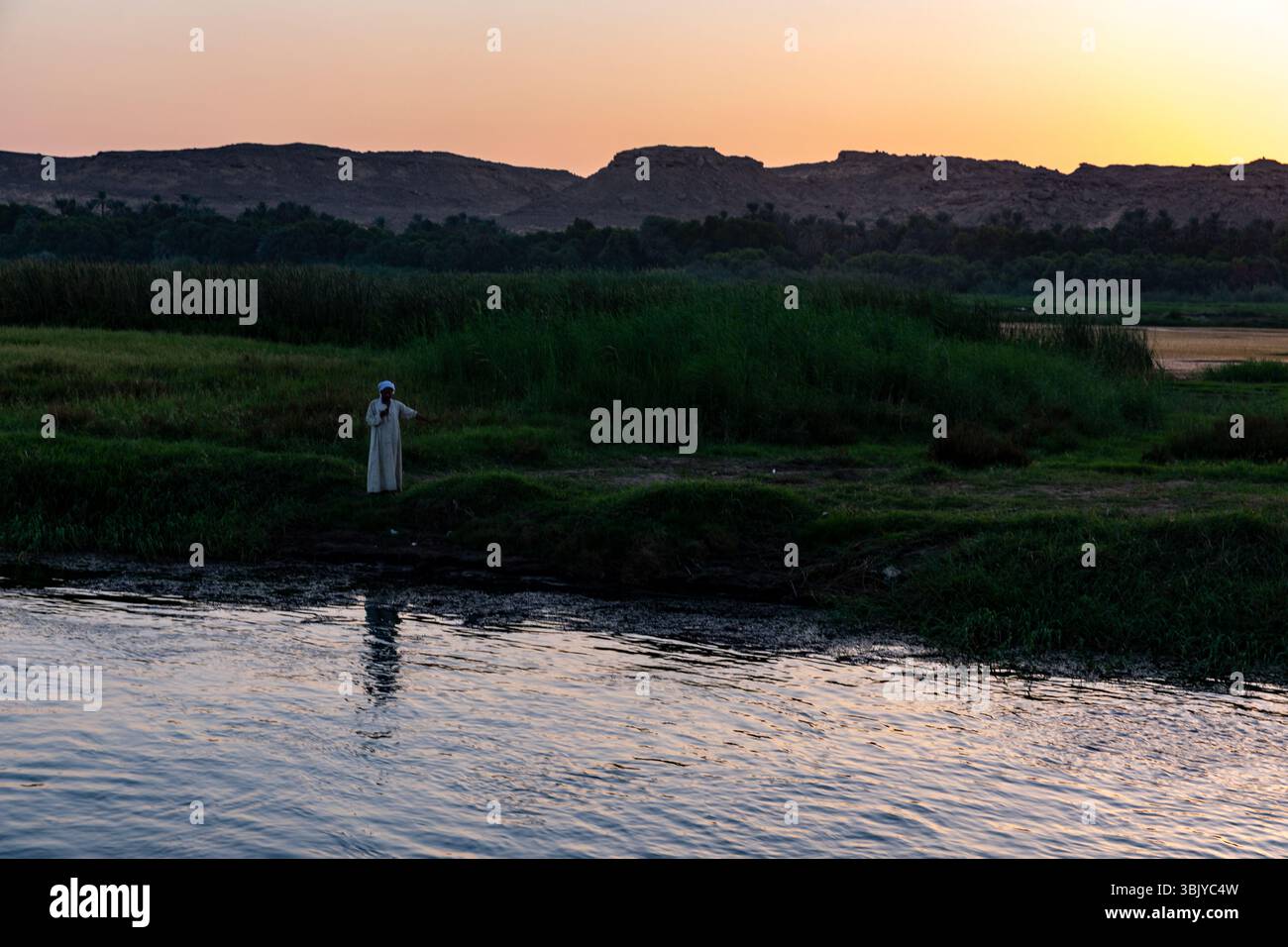 A man in traditional clothing stands by the riverbank, possibly fishing ...