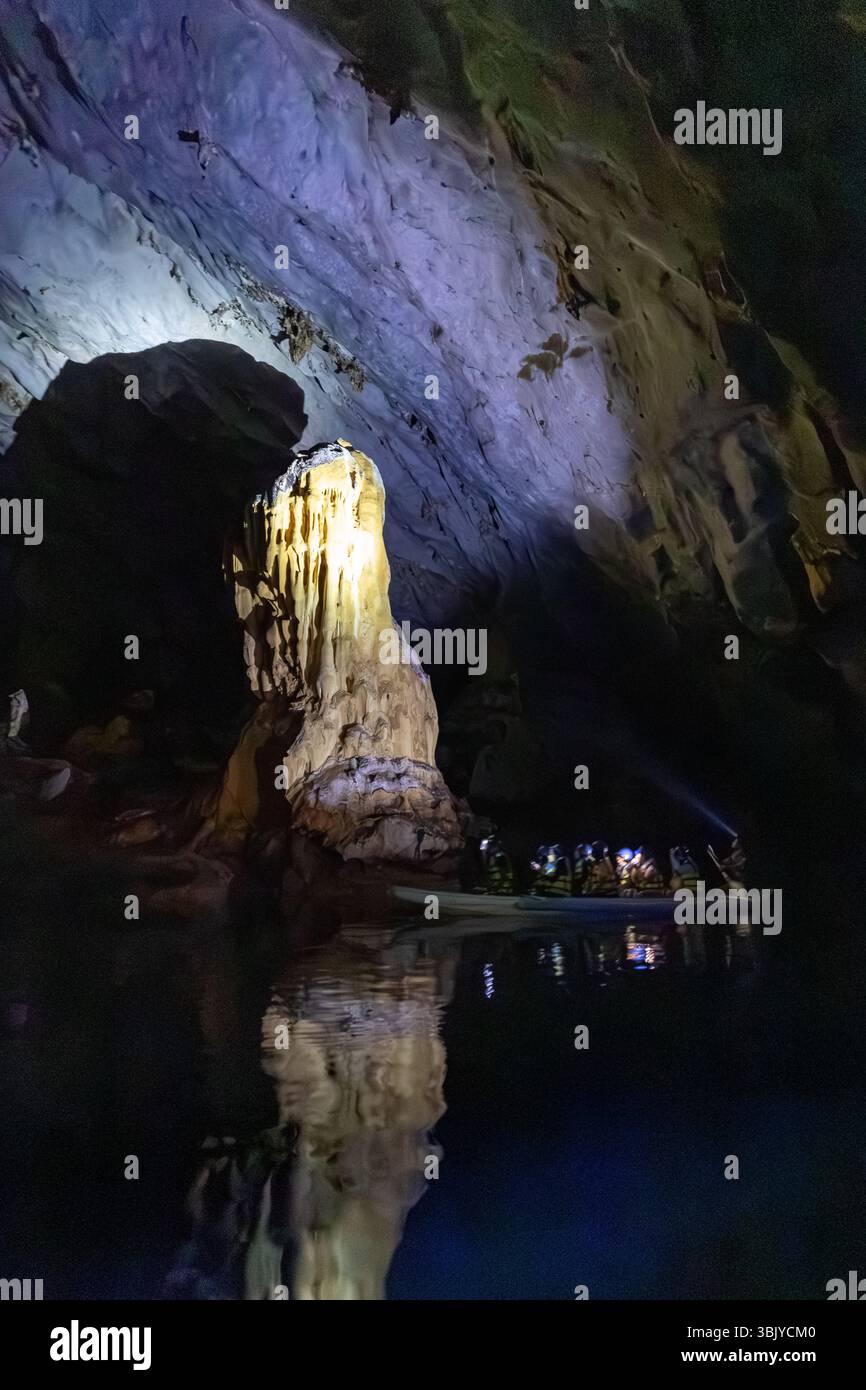 A group of people are exploring a cave by boat, with one person shining ...