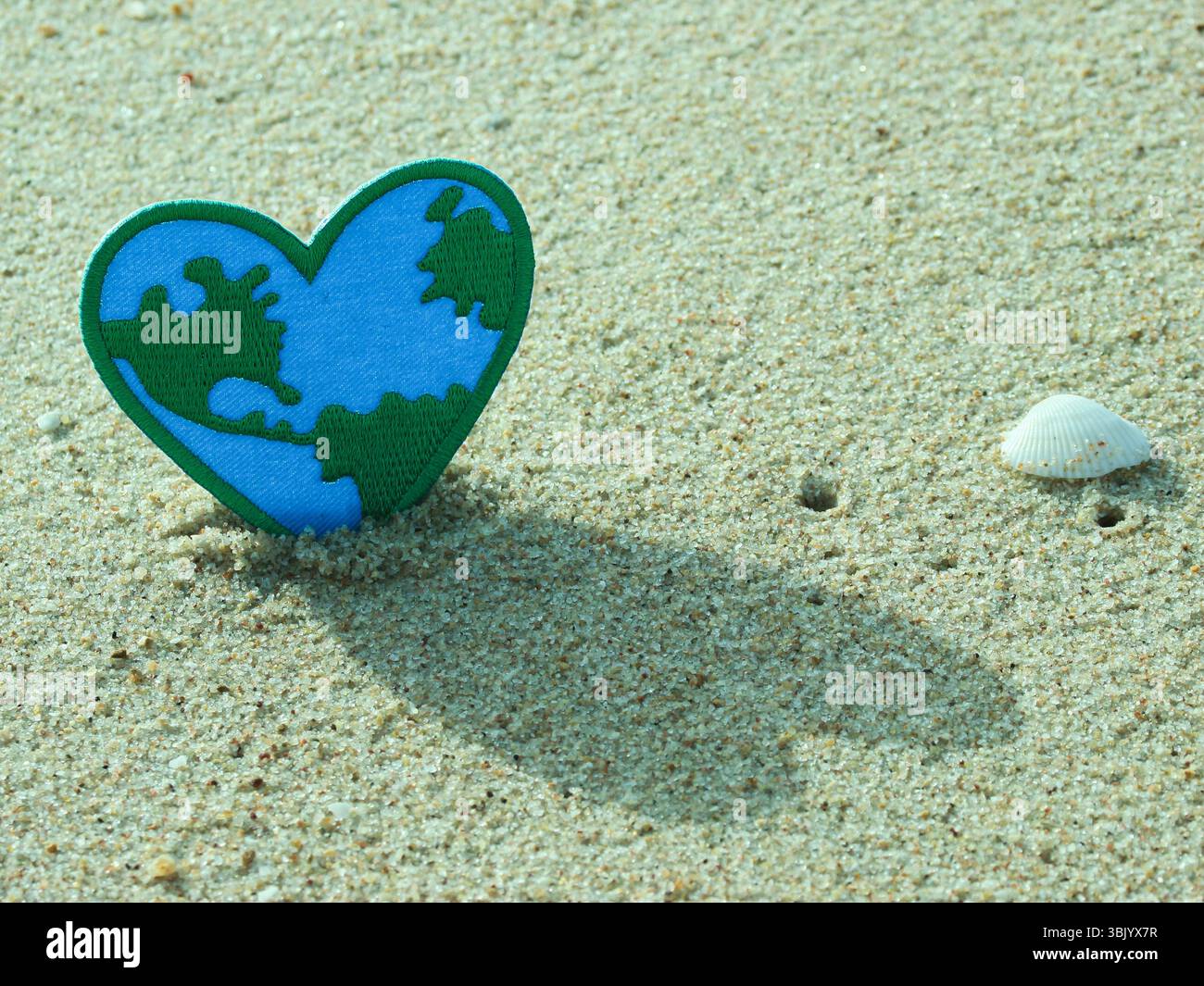 Handmade earth-pattern heart embroidery on fabric placed on beach sand ...