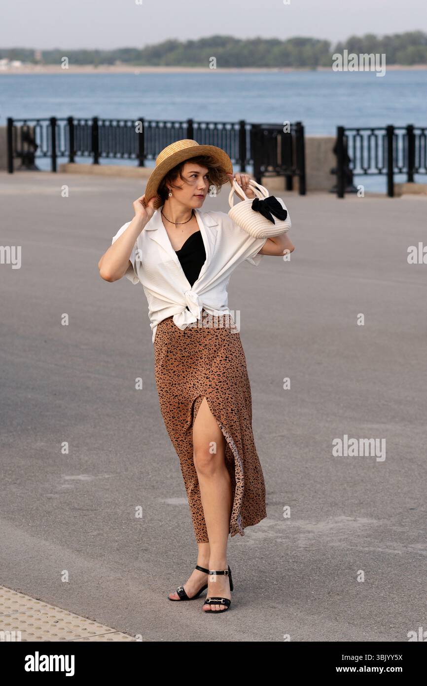 Elegant woman poses with hat by waterfront promenade evening Stock ...