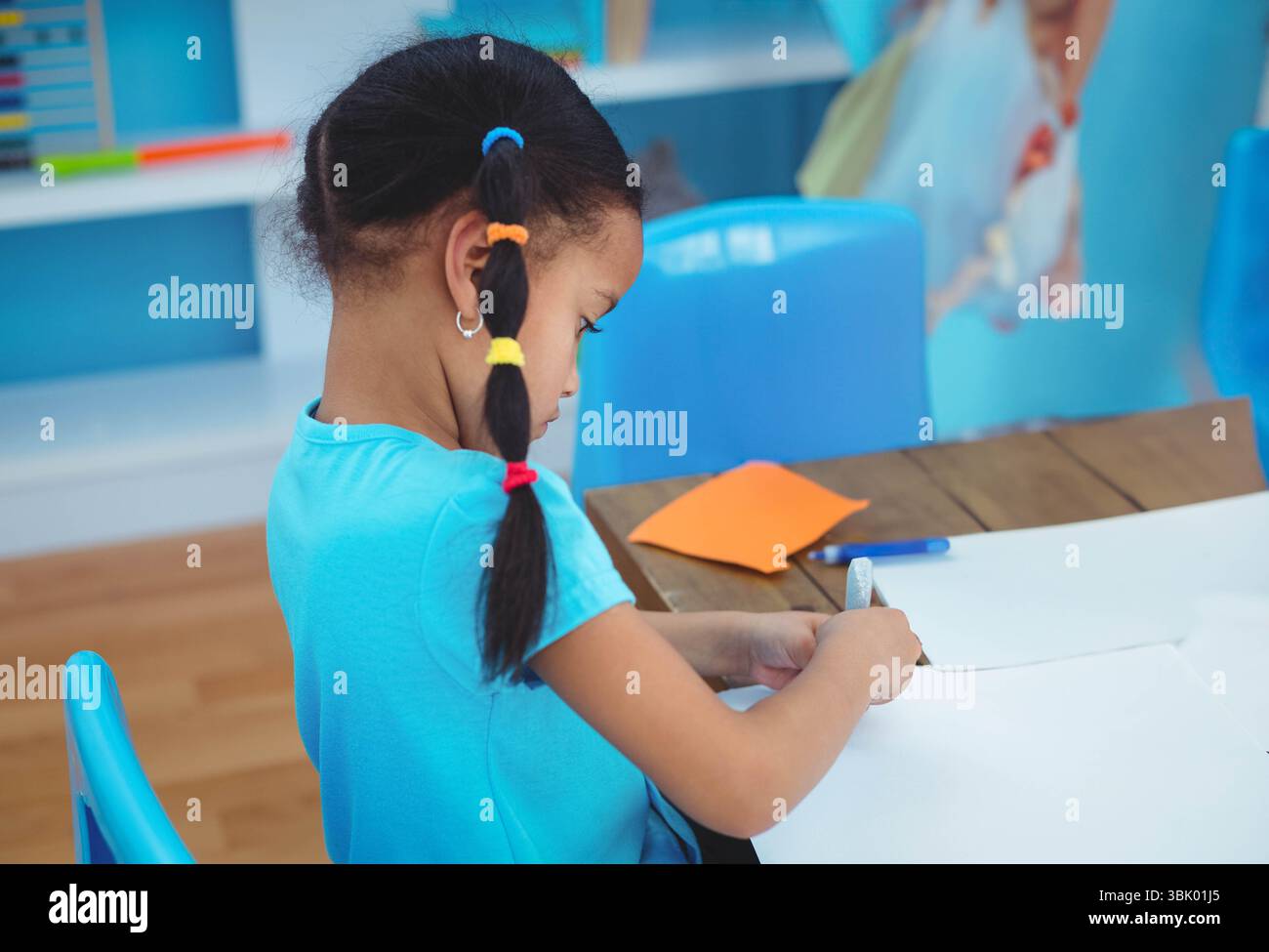 Girl drawing with marker on white paper at wooden table in classroom ...