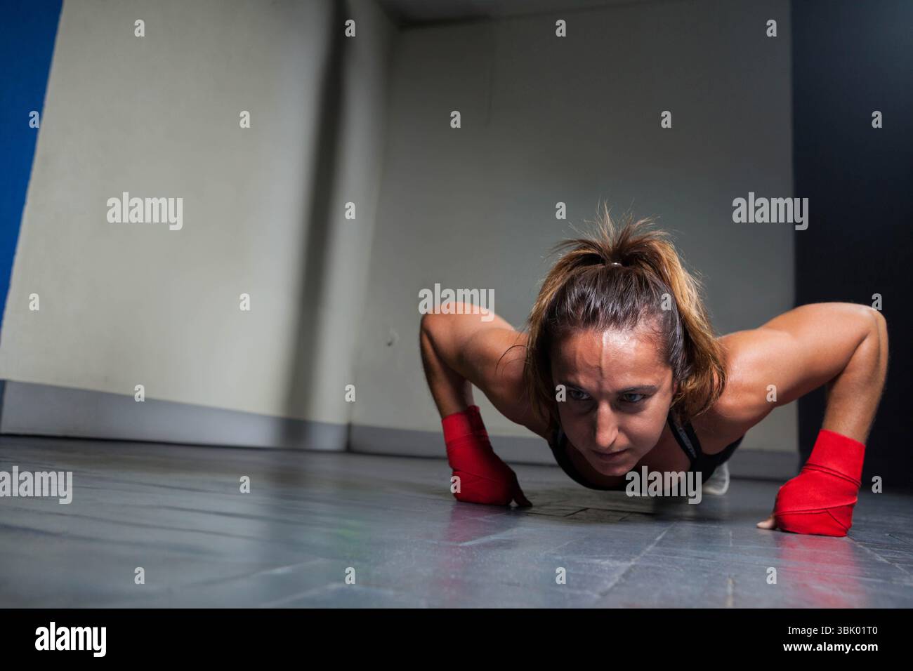 Mid adult woman in sports bra performing low push-up in training room ...