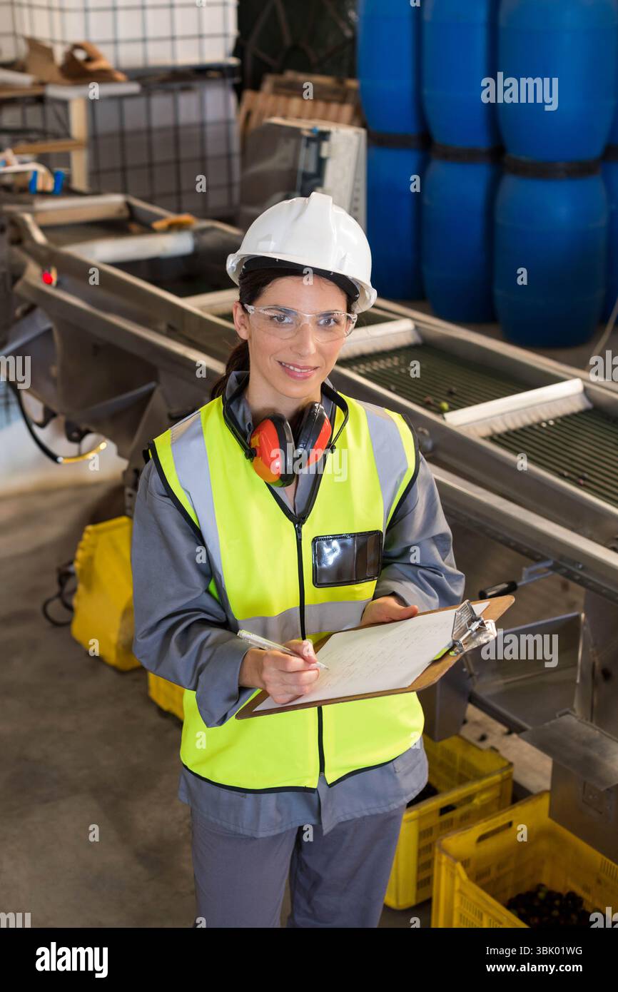 Female inspector inspecting conveyor in plant wearing helmet earmuffs ...