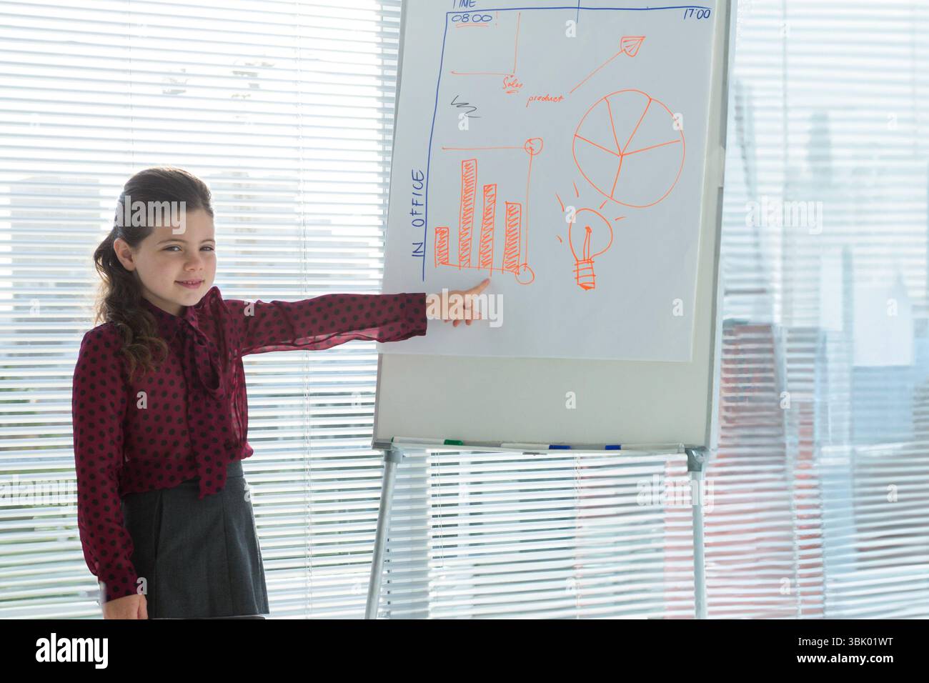 Female child standing beside flip chart in meeting room pointing to red ...