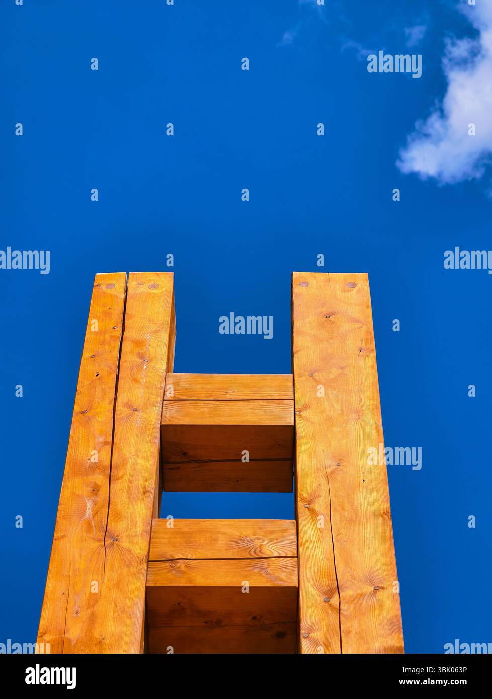 Wooden ladder reaching toward a bright blue sky with clouds ...