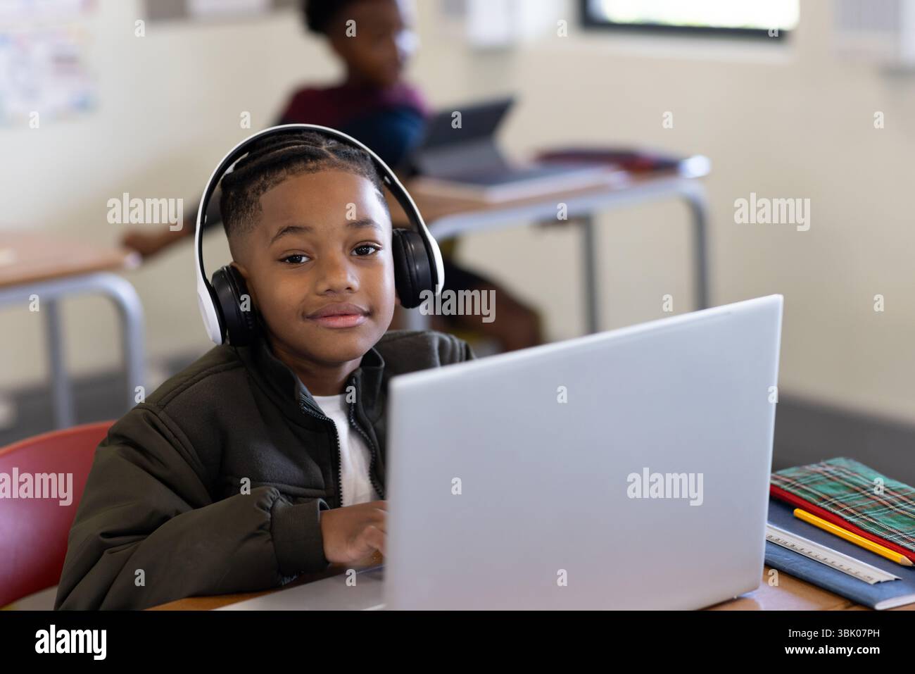 Boy wearing headphones using laptop in classroom, engaging in online ...