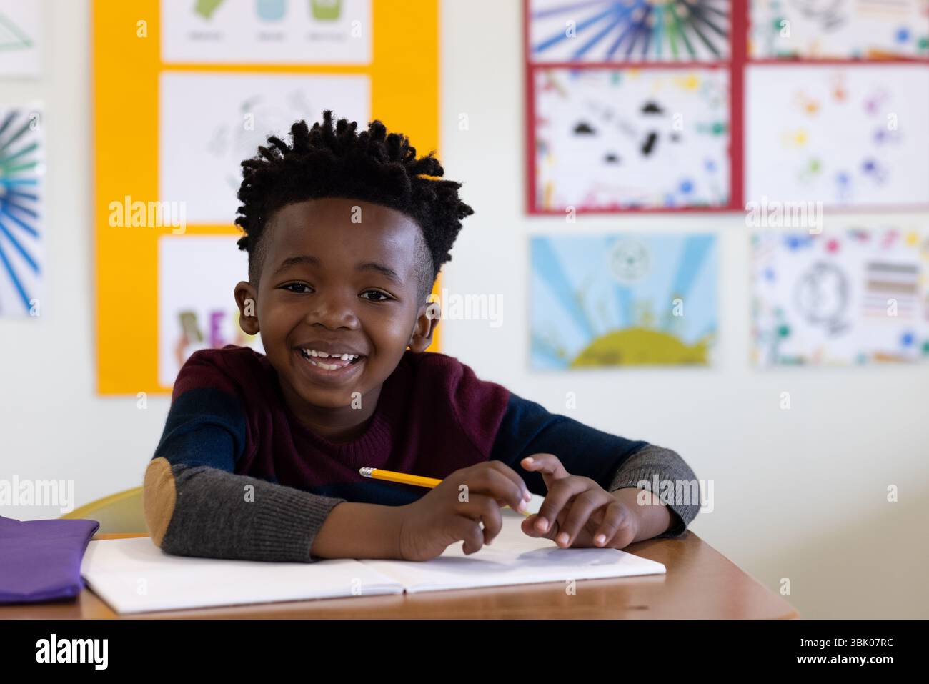 Smiling african american boy in school drawing with pencil, enjoying ...