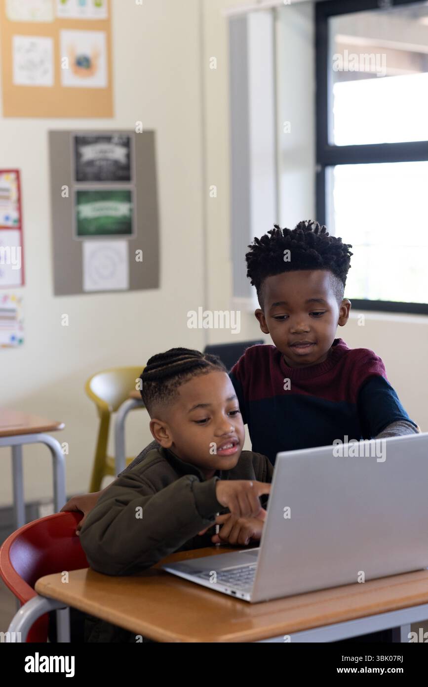 Diverse boys collaborating on laptop in classroom, learning together ...