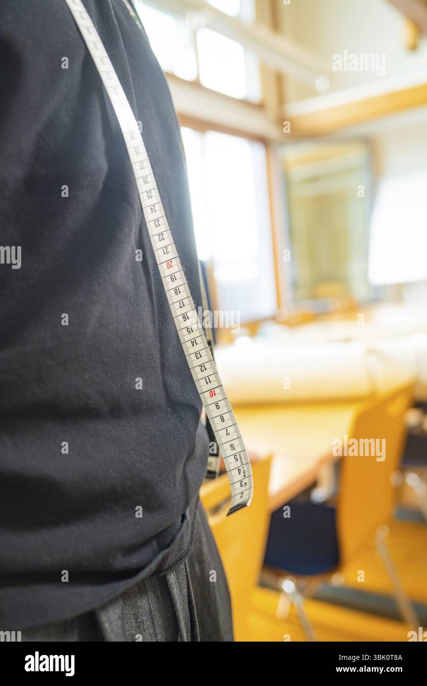 A man in a black T-shirt carries a tape measure over his shoulder in a ...