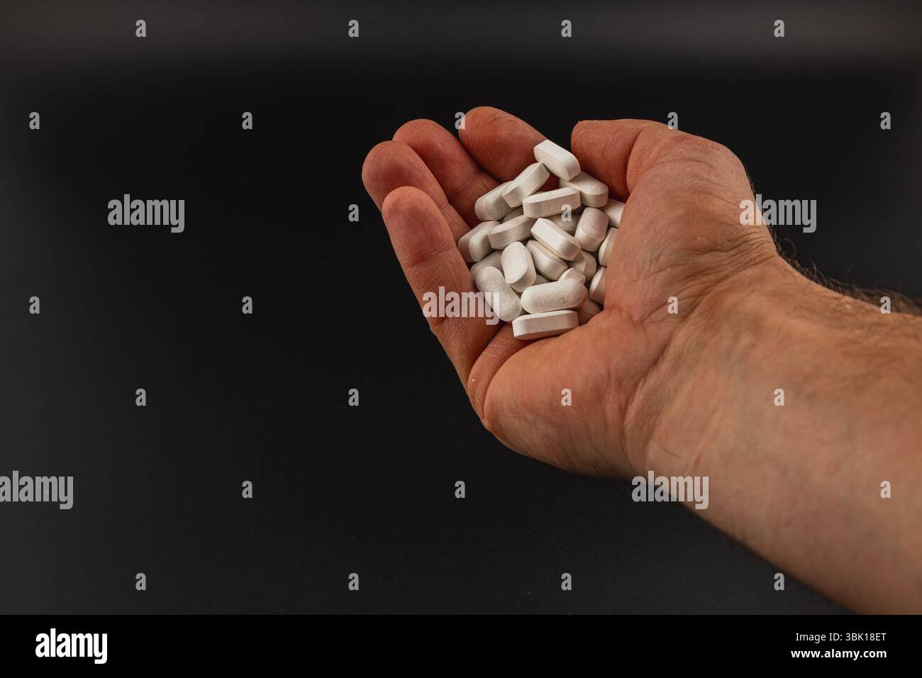 A person holds a handful of white tablets in their palm, contrasting ...