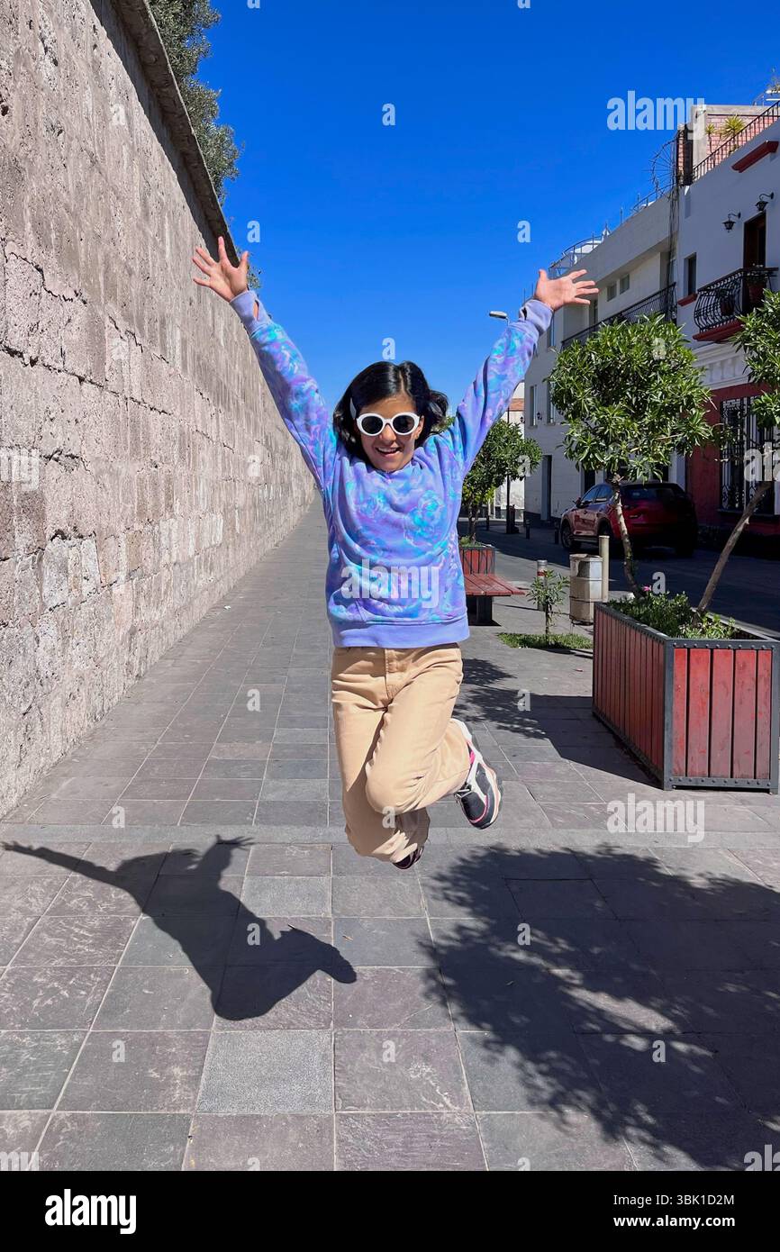 A teen is jumping in the air with her arms raised, wearing a purple ...