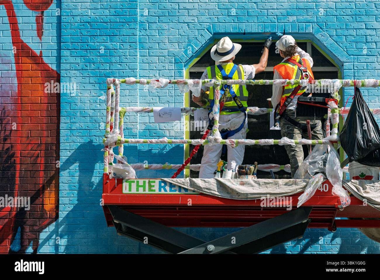 Two artists painting a colorful mural on a brick building while ...