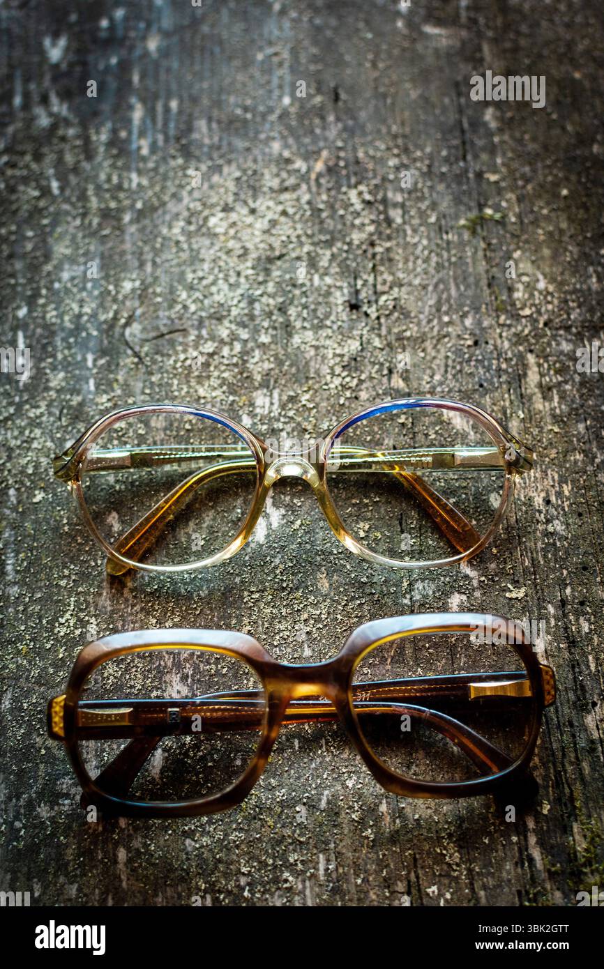 Two pairs of vintage eyeglasses rest on a weathered wooden surface ...