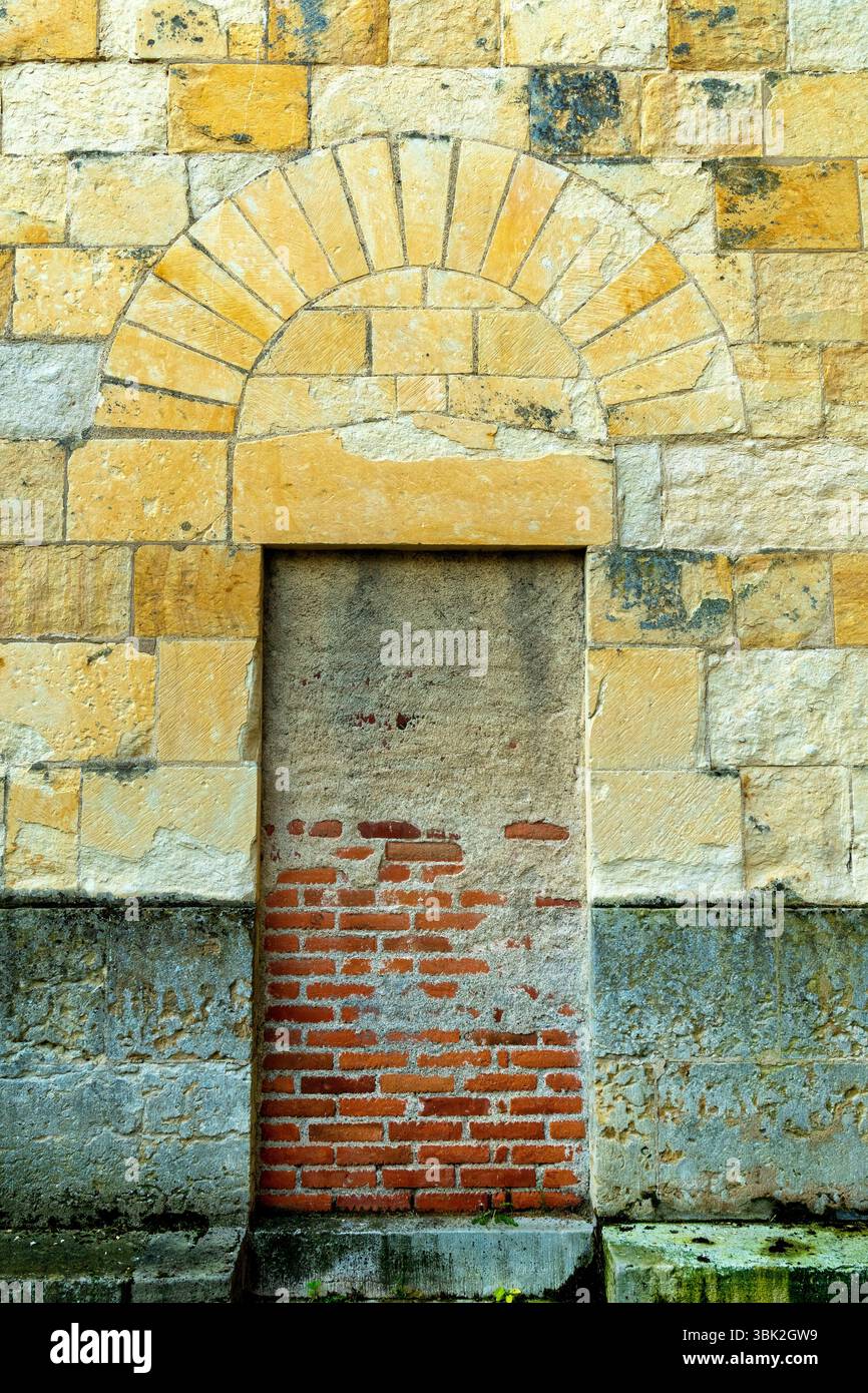 An old stone wall showcases a prominently arched doorway, leading to an ...