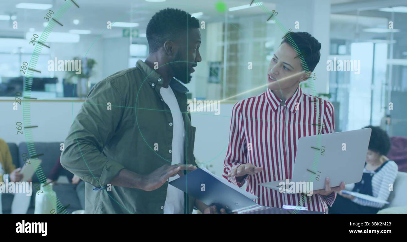 Two professionals discussing work over document folder and laptop in open plan office, with sofa ...