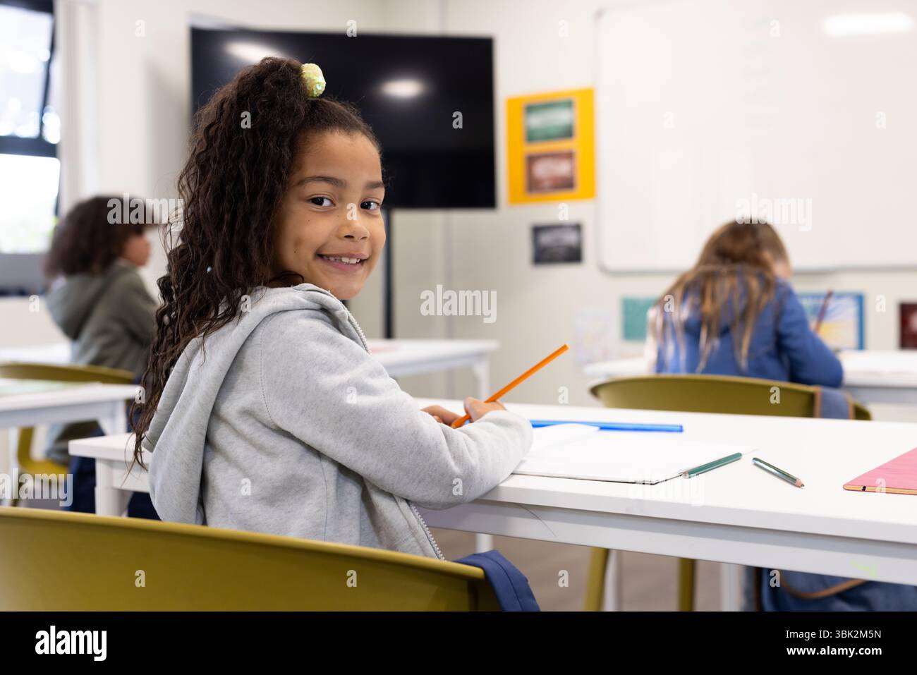 Smiling girl in classroom writing with pencil, enjoying school ...