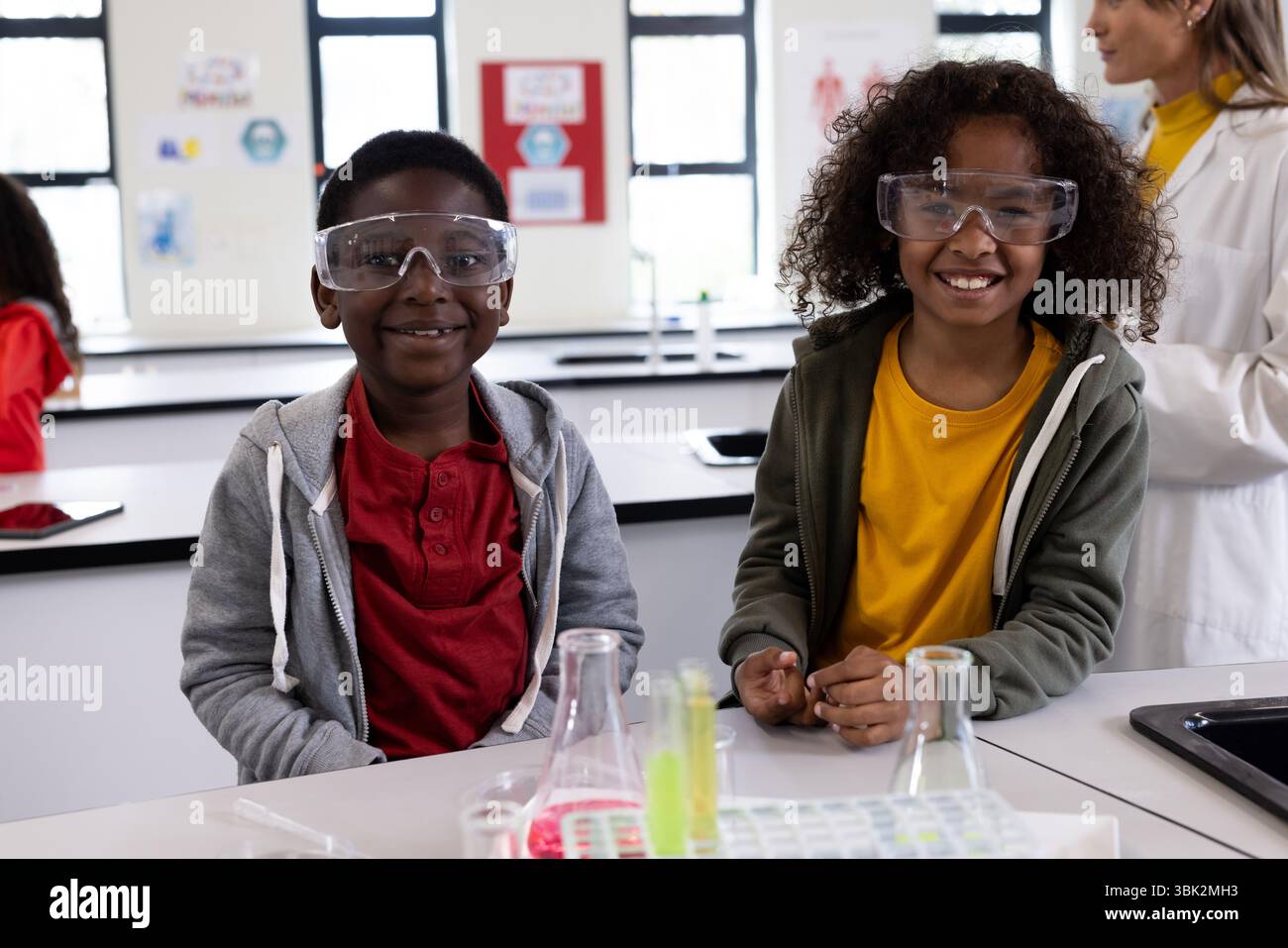 Smiling diverse students wearing safety goggles in school science lab ...