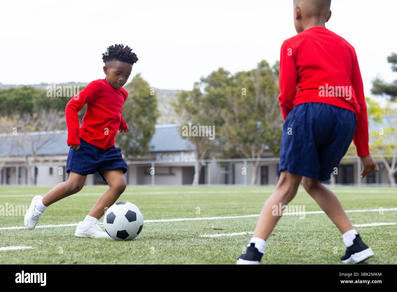 Diverse boys playing soccer on school field, wearing red shirts and ...