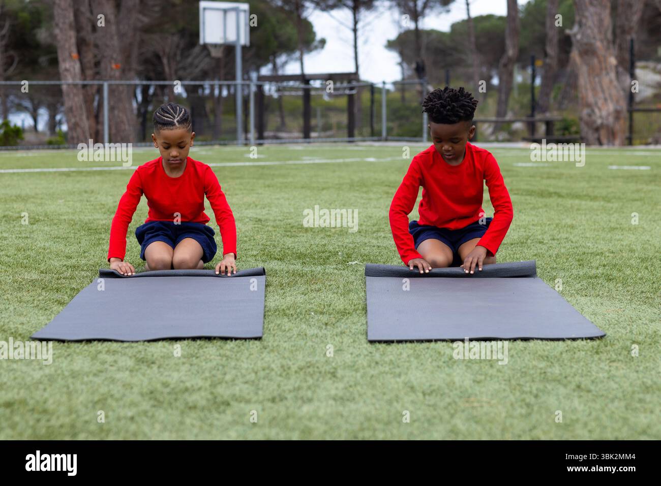 Diverse boys rolling yoga mats on grass, preparing for outdoor school ...