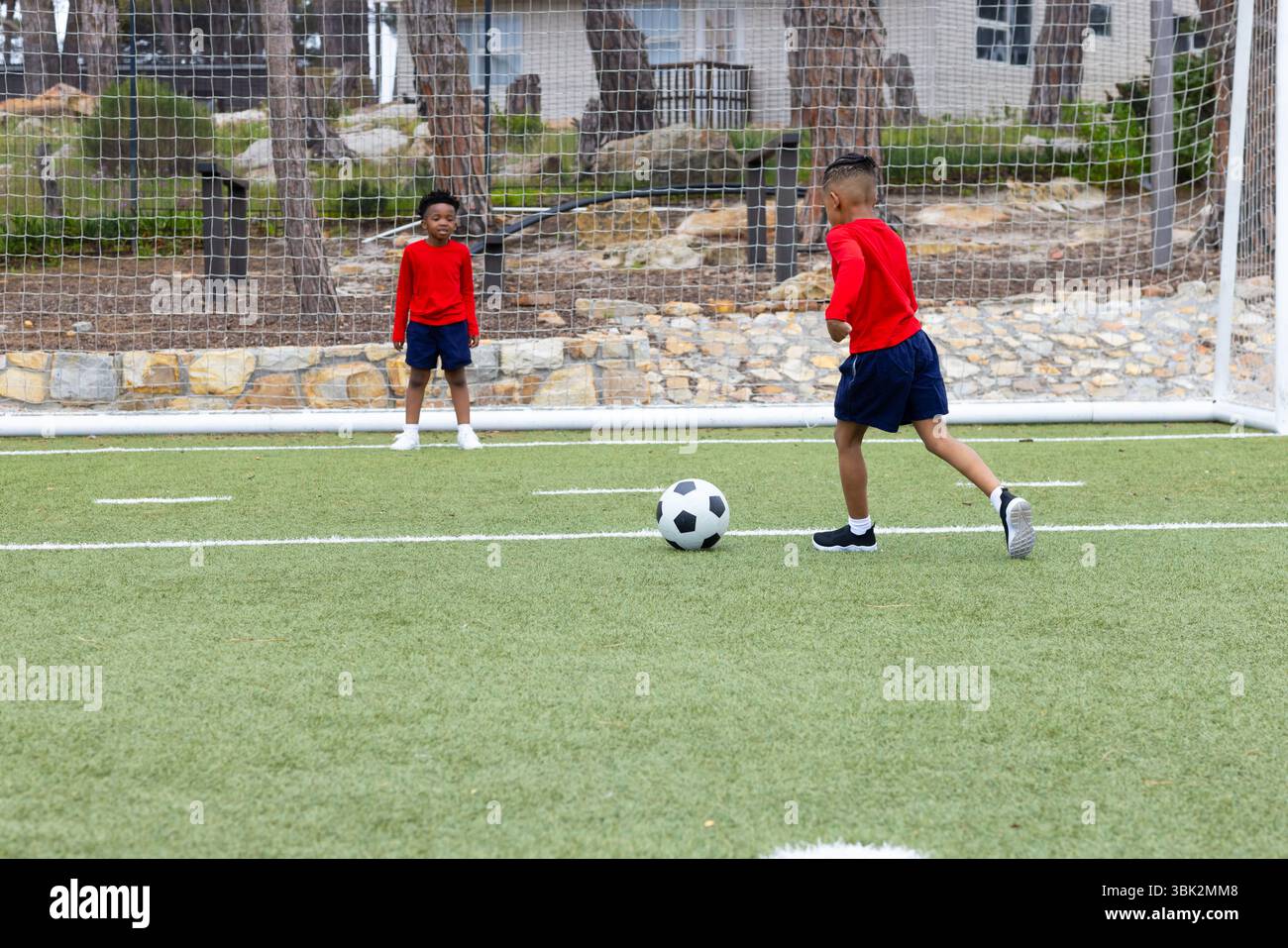 Diverse boys playing soccer on field, one kicking ball towards goal ...