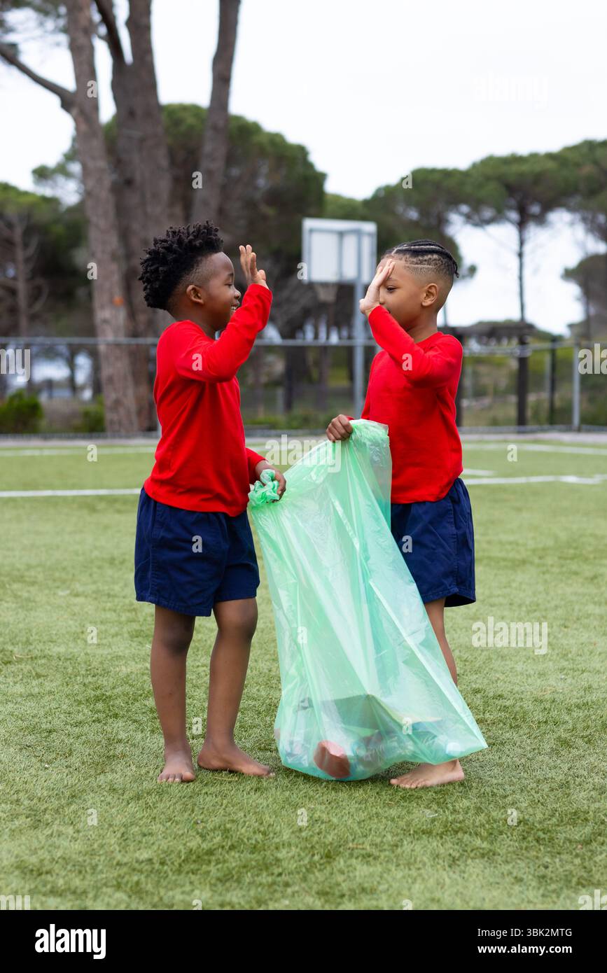 Diverse boys in school uniforms cleaning up park, celebrating teamwork ...