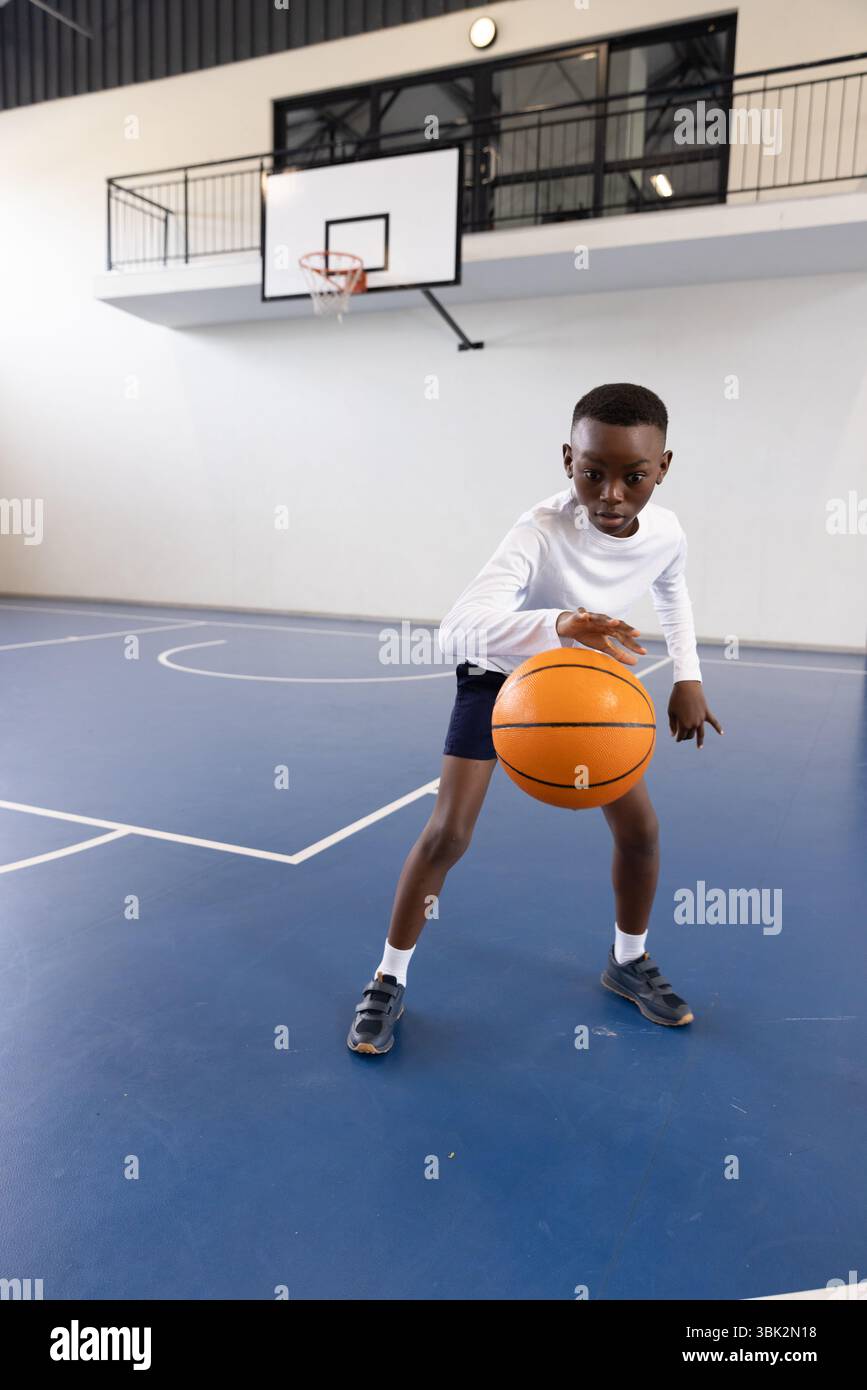 African american boy playing basketball in school gym, dribbling ball ...